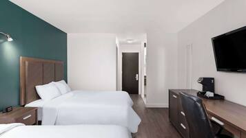 Quarto de hotel com duas camas, uma escrivaninha, uma cadeira, uma televisão e uma máquina de café.