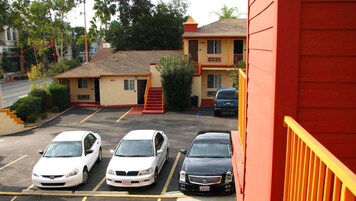Um estacionamento com três carros estacionados em frente a um edifício com fachada vermelha e uma varanda.