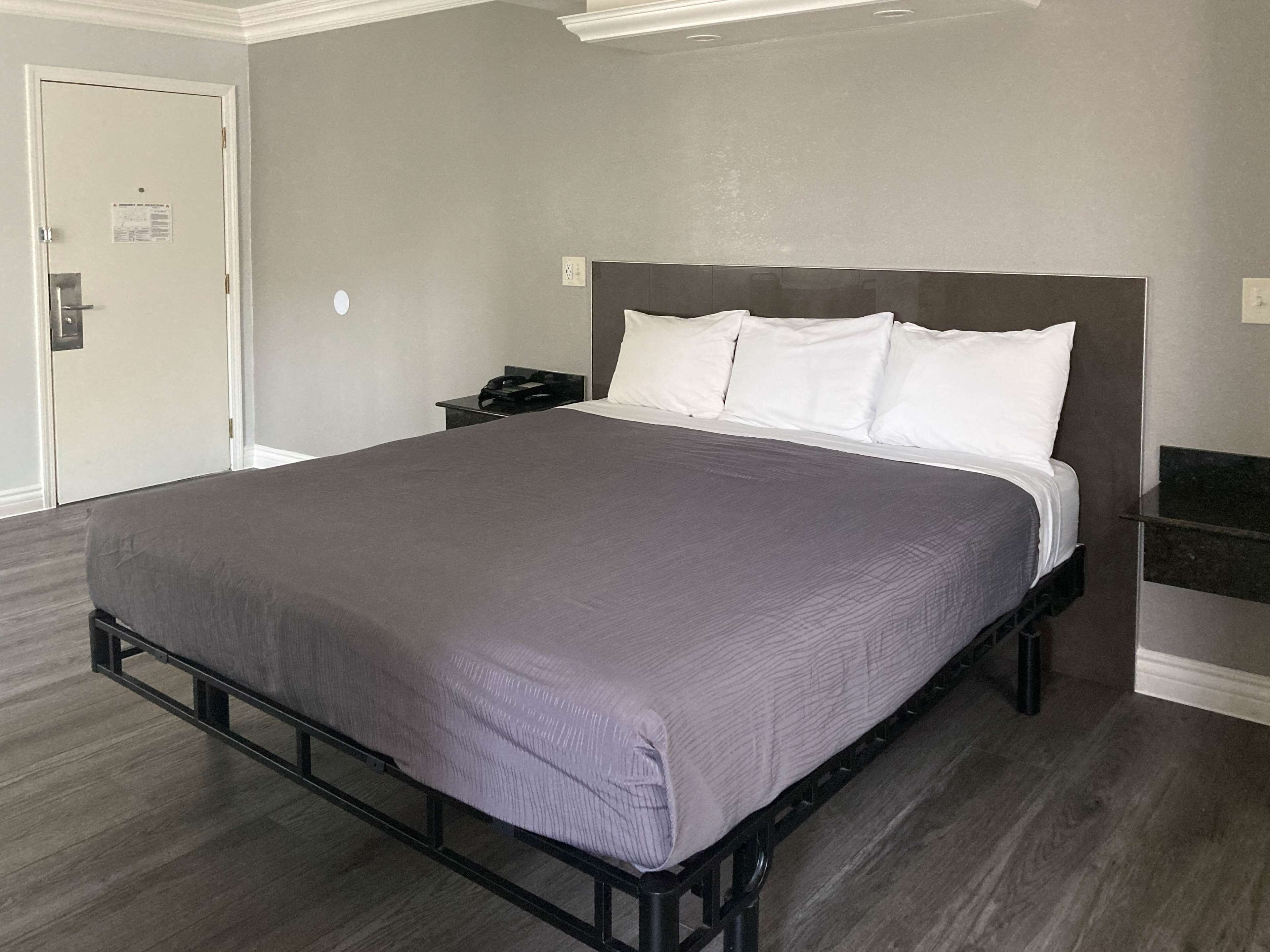 Quarto de hotel moderno com uma cama grande, uma mesa de cabeceira e chão de madeira escura.