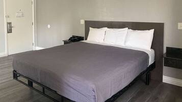 Quarto de hotel moderno com uma cama grande, uma mesa de cabeceira e chão de madeira escura.