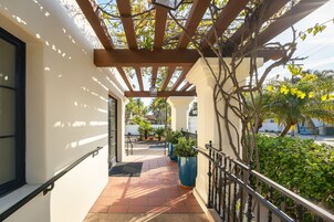 Uma área externa coberta com piso de azulejos, pérgola de madeira e plantas em vasos.