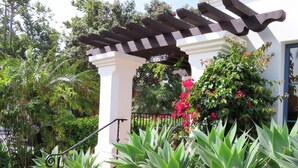 Uma área externa coberta com pérgola, escadas que levam a uma porta identificada como 