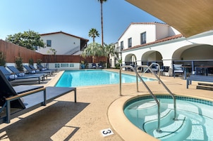 Uma área de piscina com espreguiçadeiras, uma banheira de hidromassagem e um edifício com arcos.
