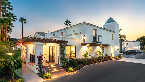 Um edifício branco com uma placa indicando "Mason Beach Inn" e uma varanda com guarda-corpo.