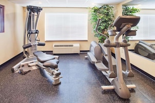Uma academia com máquinas de cardio, um banco e um aparelho de ar condicionado fixado na parede.
