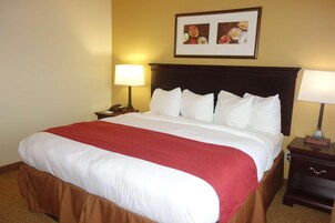 Quarto de hotel com uma cama grande, duas mesas de cabeceira, um criado-mudo, uma luminária e um quadro na parede.