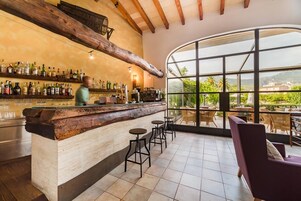 Área de bar com balcão de madeira, banquetas e uma grande janela com vista para o verde e edifícios.