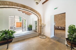Um hall amplo com uma grande porta arqueada, balcão de recepção, candelabro e sofá com almofadas estampadas.