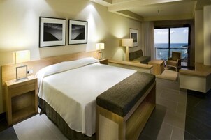 Quarto de hotel com uma cama grande, uma escrivaninha, uma cadeira e vista para o oceano.