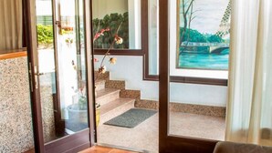 Quarto com sofá de couro marrom, porta de vidro que dá para uma varanda e vista para uma piscina.