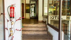 Entrada de um hotel com um extintor, um vaso de plantas e uma escadaria que leva ao interior.
