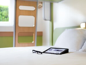 Uma cama com um tablet e óculos, uma parede verde e uma janela com vista.
