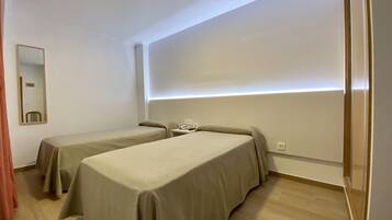 Quarto de hotel com duas camas de solteiro, mesa de cabeceira com telefone, espelho e iluminação na parte superior do teto.