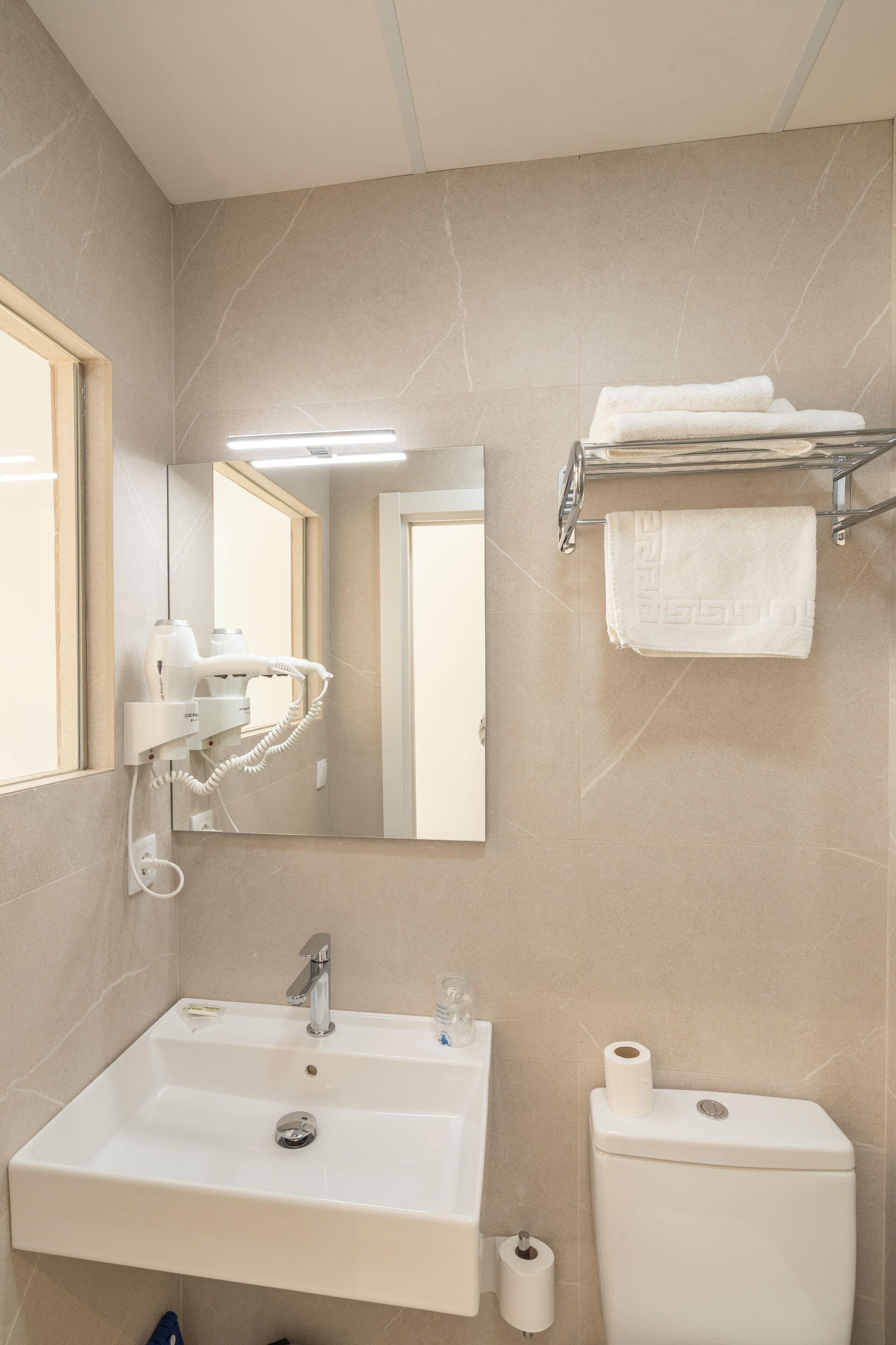 Casa de banho com lavatório branco, espelho e porta-toalhas.