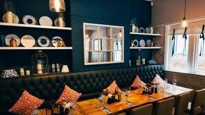 Uma sala de jantar com uma mesa de madeira comprida posta para seis pessoas, rodeada por assentos acolchoados.