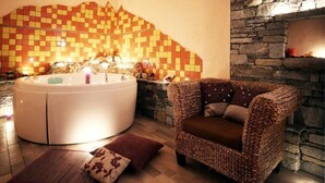 Um quarto aconchegante com lareira de pedra, uma banheira redonda e uma cadeira de vime.