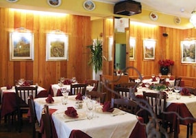 Restaurante com paredes revestidas de madeira, quadros decorativos e mesas com toalhas brancas e guardanapos vermelhos.