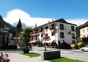 Hotel com fachada branca, várias varandas floridas e montanhas ao fundo.