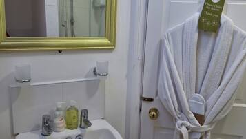 Casa de banho com uma pia branca, um espelho com moldura dourada e um roupão pendurado na porta, com uma placa que diz 'Por favor, limpe o quarto, obrigado'.