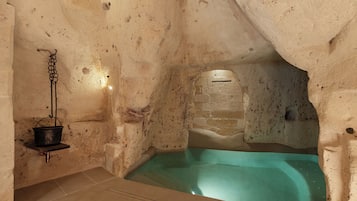 Piscina interna com paredes de pedra e um balde pendurado.