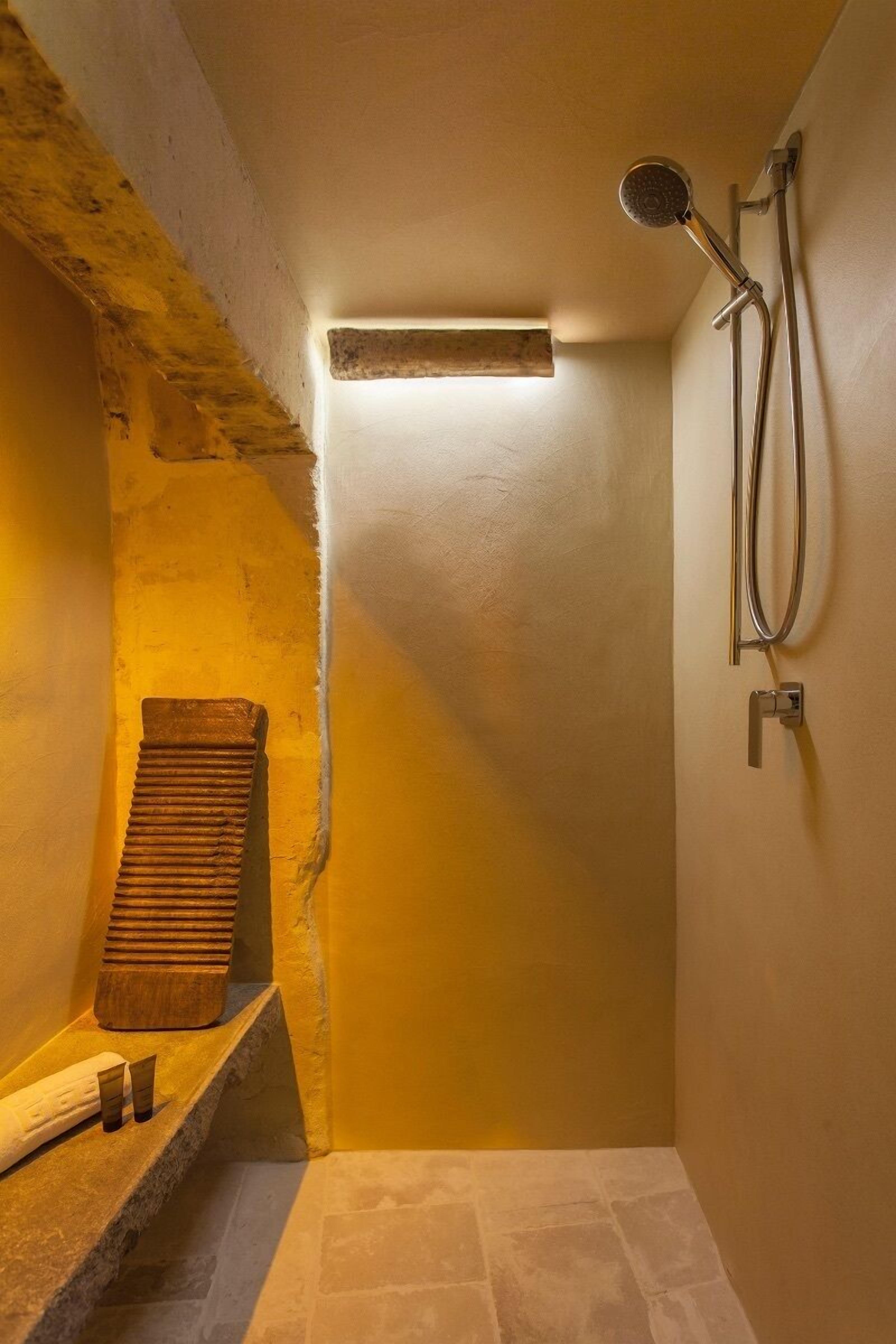 Um banheiro pequeno e moderno com chuveiro, um banco de madeira e uma luminária.