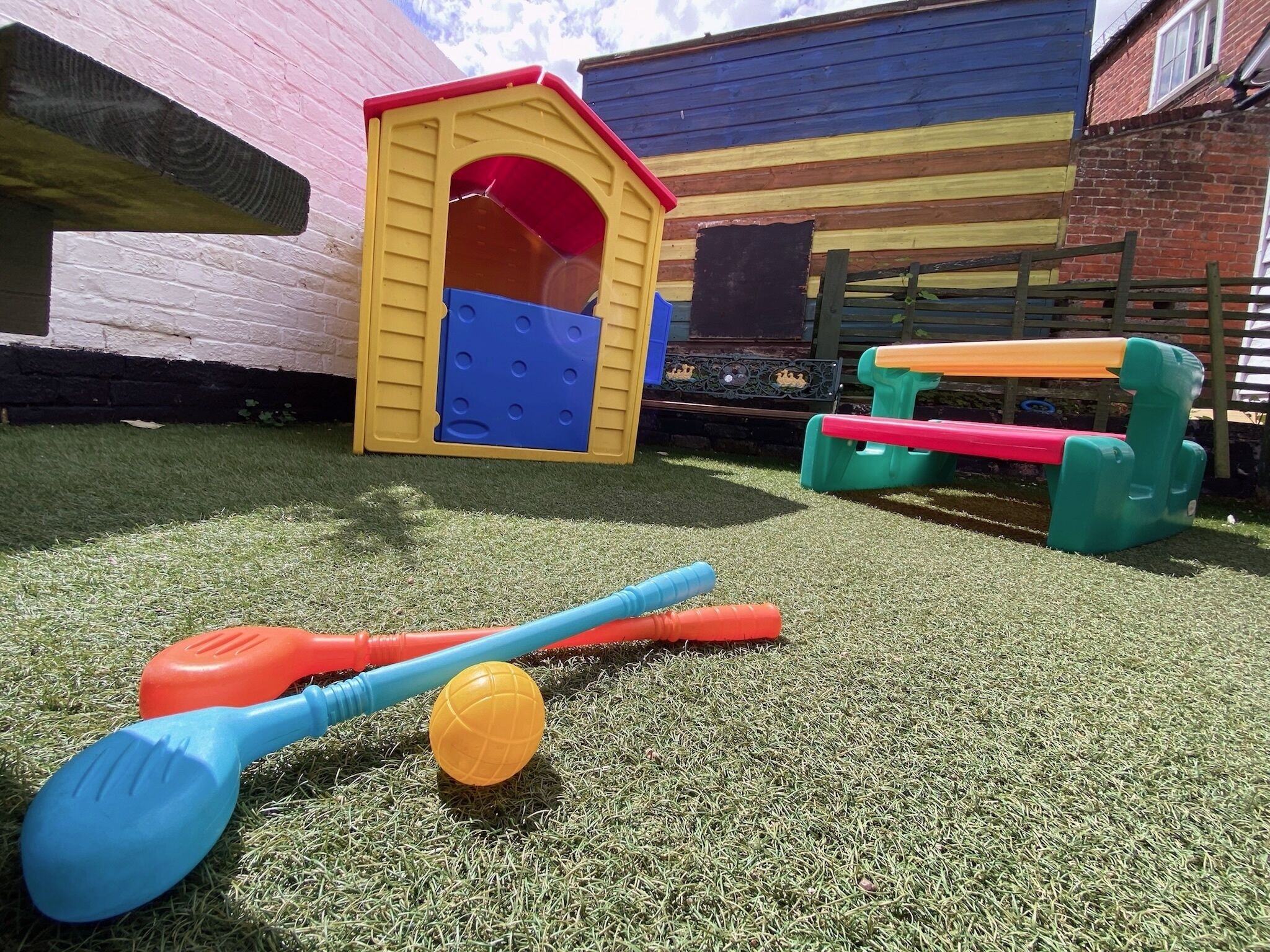 Uma área de recreação infantil com uma casinha, escorrega e diversos brinquedos sobre grama sintética.