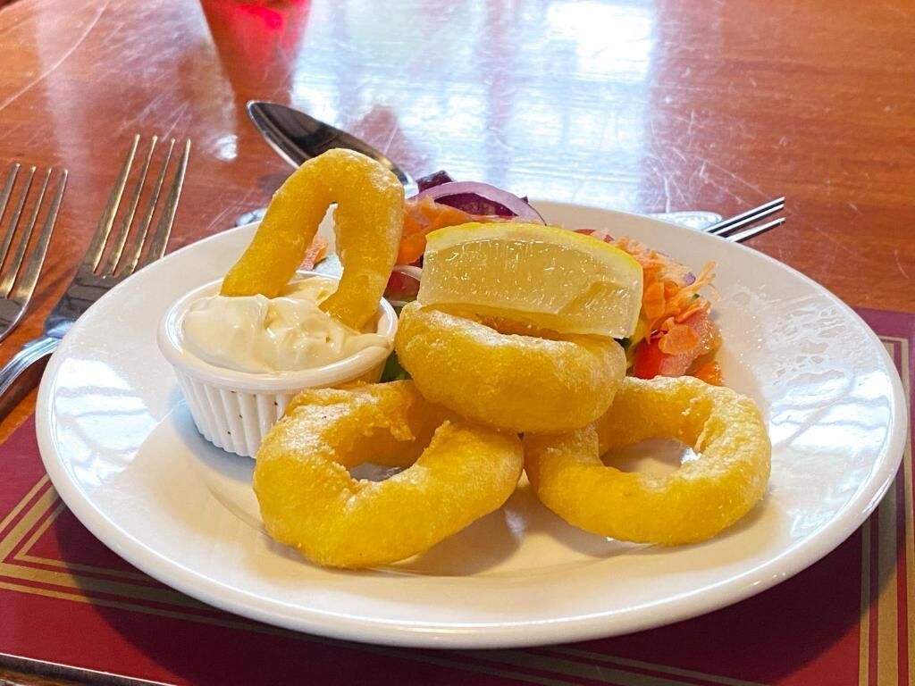 Um prato com anéis de cebola, um gajo de limão e uma pequena tigela de molho.