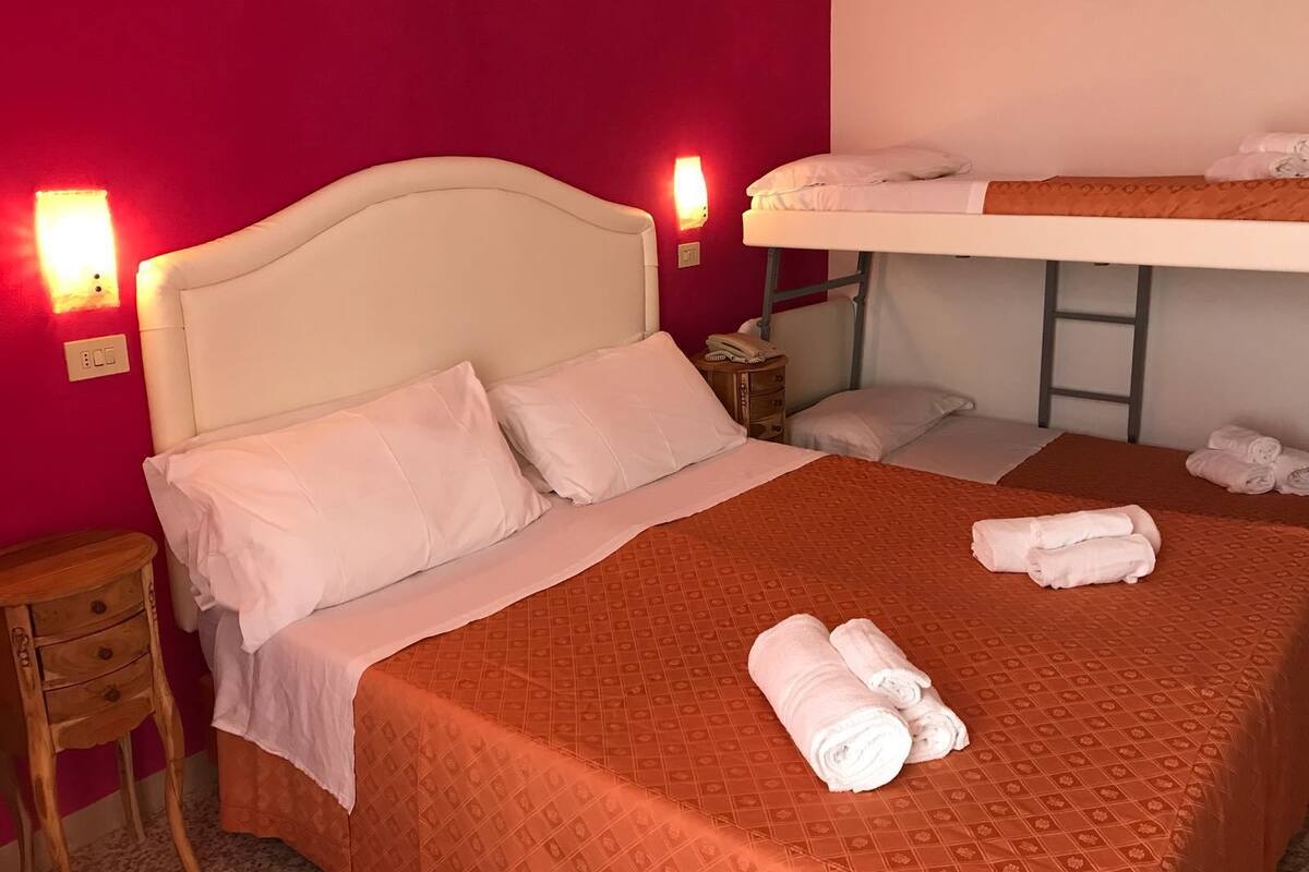 Quarto de hotel com uma cama de solteiro, uma cama beliche e uma mesa de cabeceira com abajur.