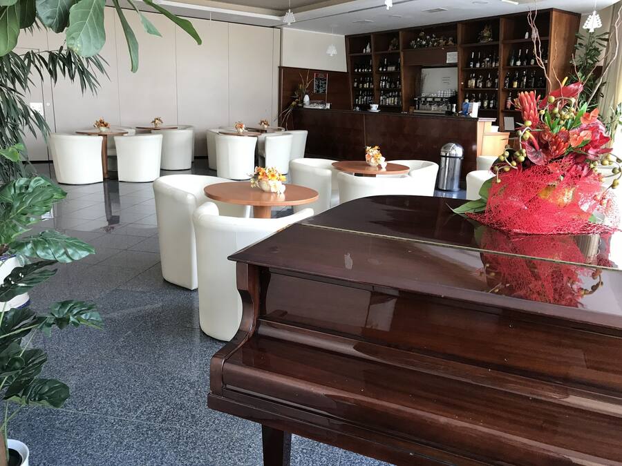 Uma área de estar moderna com um piano de madeira brilhante, assentos acolchoados brancos e um bar com prateleiras cheias de garrafas.