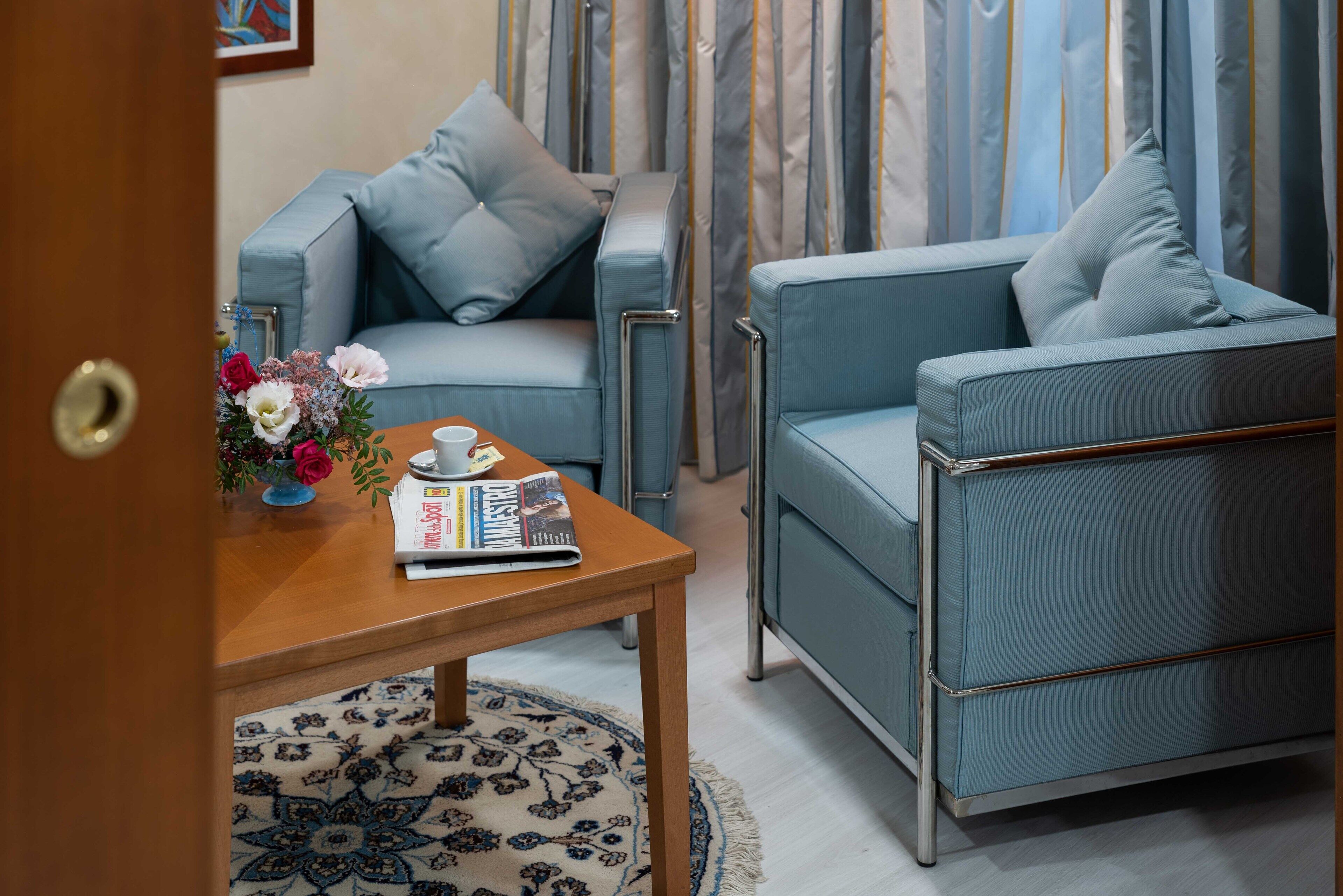 Um quarto com um sofá azul, uma mesa de centro de madeira com uma revista e um tapete estampado.