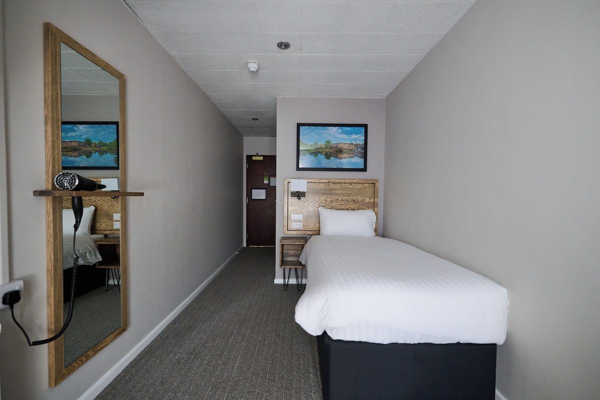 Quarto de hotel com cama, escrivaninha, cadeira, espelho e um quadro na parede.