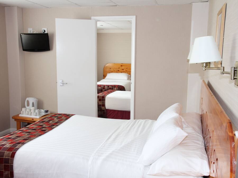 Quarto de hotel com cama, mesa de cabeceira com luminária e televisão na parede.