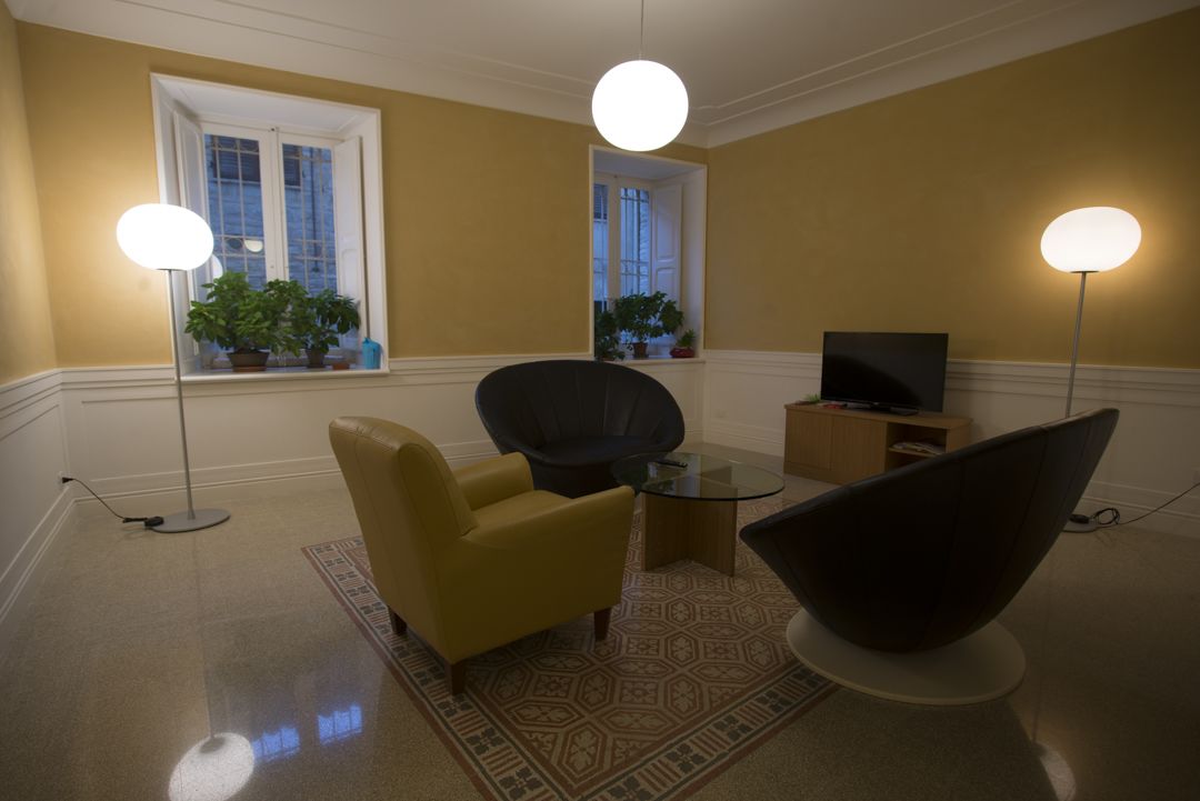 Uma sala de estar moderna com uma parede amarela, uma mesa redonda, uma poltrona amarela, uma cadeira preta, um sofá preto e duas luminárias de chão.