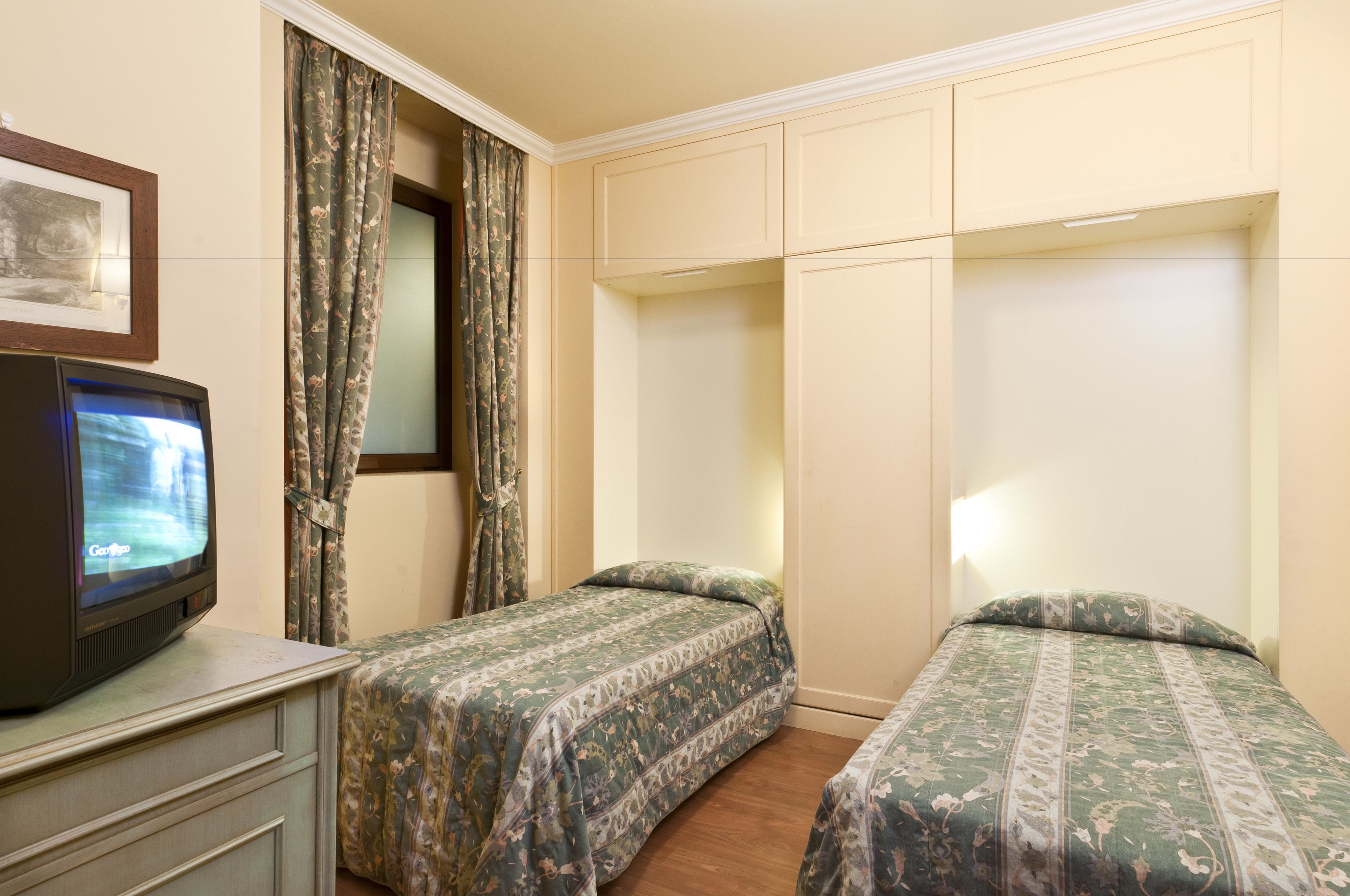 Quarto de hotel com duas camas, uma televisão e um espelho.