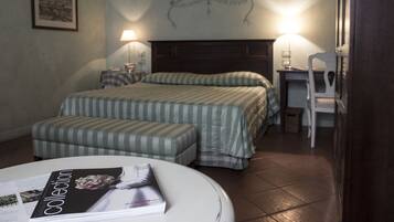 Quarto de hotel com duas camas, uma escrivaninha e uma cadeira. Há um quadro na parede e um abajur na escrivaninha.