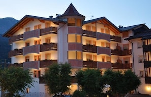 Um hotel com vários andares, varandas, uma torre central e montanhas ao fundo.