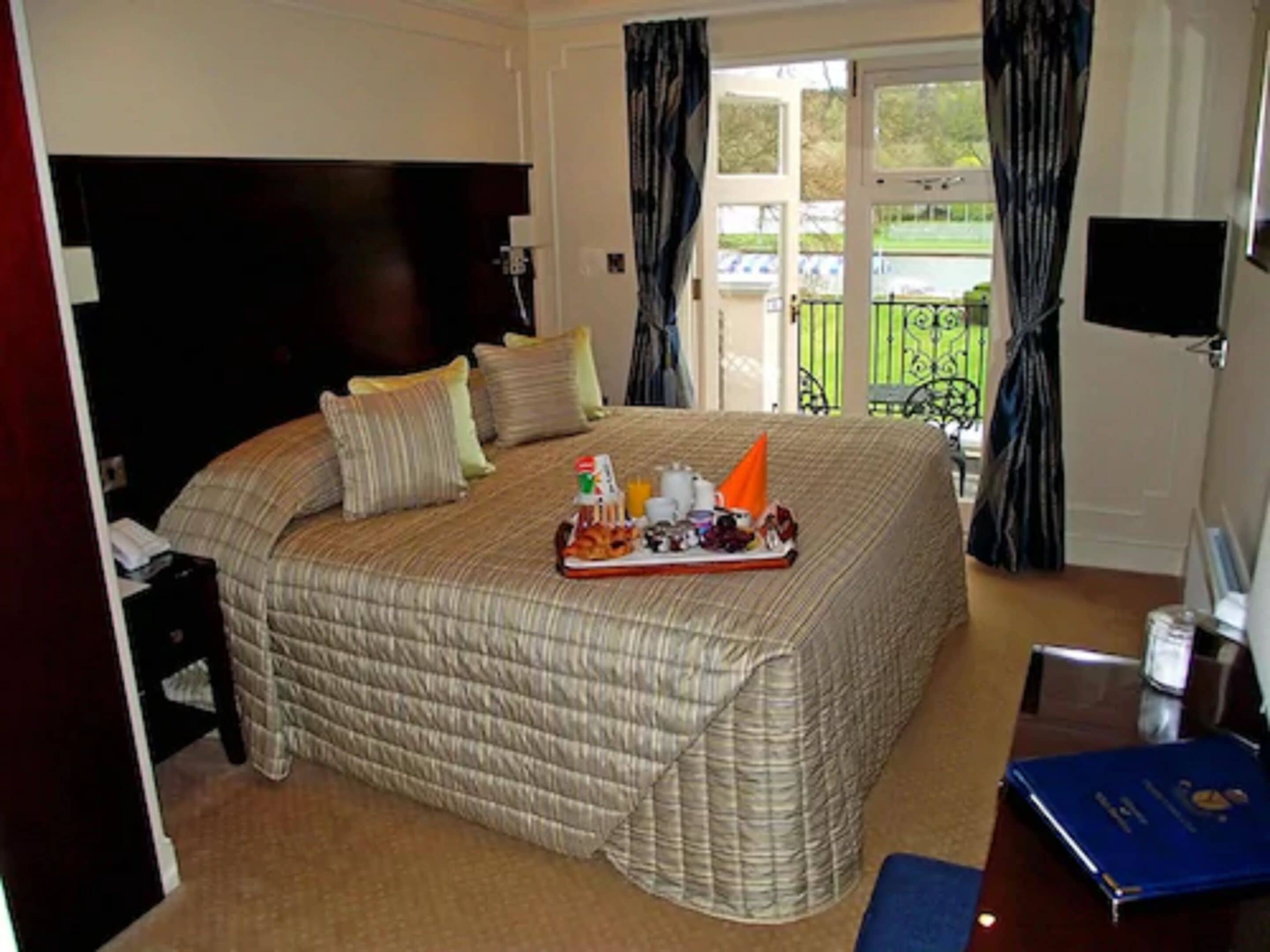 Quarto de hotel com uma cama grande, bandeja de itens de café da manhã, televisão e vista para o exterior.