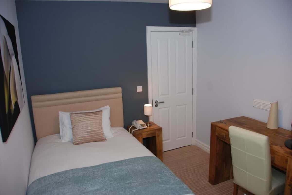 Quarto com cama, mesa de cabeceira, escrivaninha, cadeira e porta.