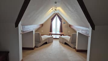 Quarto de sótão amplo, com pé direito alto, teto inclinado, uma janela grande com cortinas e um banco de madeira.