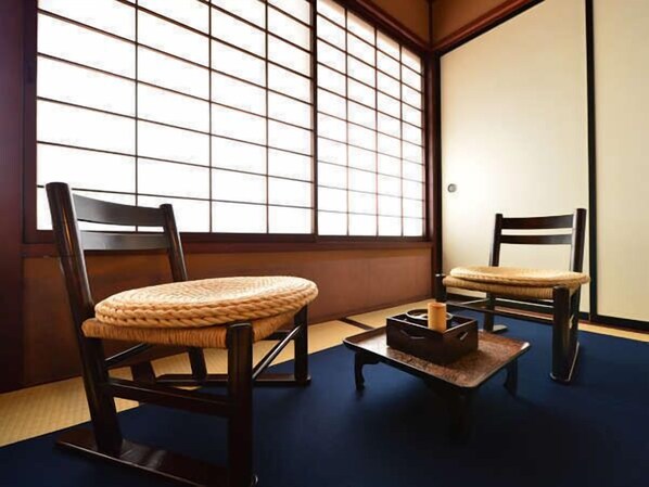 Um quarto japonês tradicional com tatames, duas cadeiras de madeira, uma mesa pequena e uma porta deslizante.