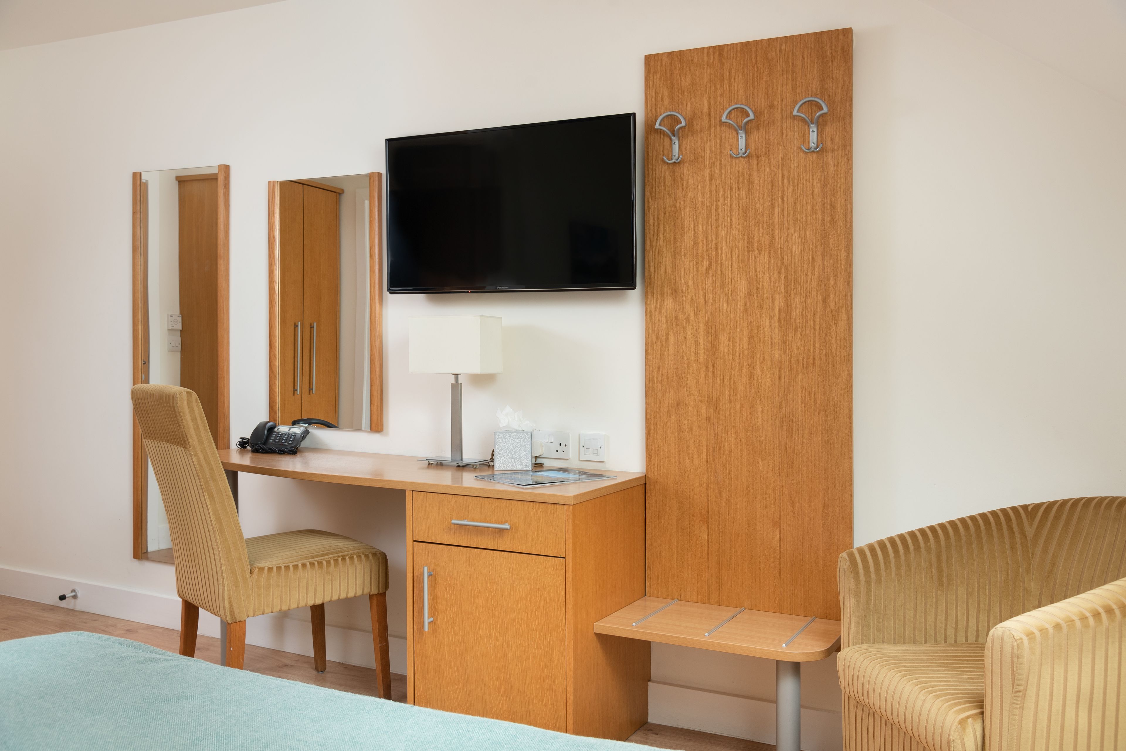 Quarto de hotel com escrivaninha de madeira, televisão, cadeira, cama e guarda-roupa.