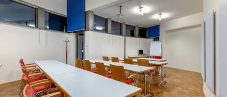 Uma sala de conferências com várias mesas e cadeiras, janelas amplas e um quadro branco.