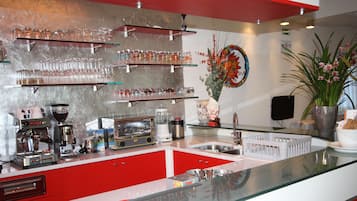 Uma área de bar moderna com prateleiras de vidro exibindo diversos copos, uma máquina de café e um vaso decorativo com flores.