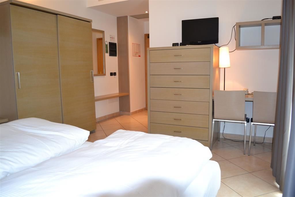 Quarto de hotel com cama, escrivaninha, televisão e guarda-roupa.