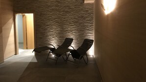 Quarto com parede de pedra, duas poltronas e uma porta de madeira.