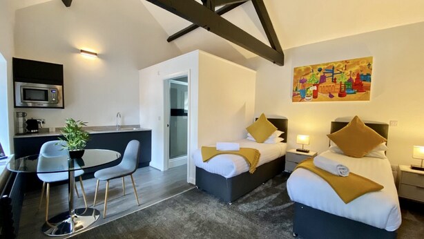 Quarto de hotel moderno com duas camas, área de jantar e cozinha.