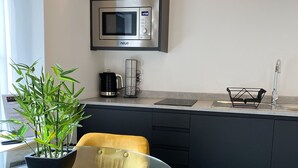 Uma cozinha moderna com micro-ondas embutido, uma pia e um pequeno espaço de jantar com duas cadeiras amarelas e uma mesa de vidro.