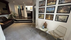 Uma sala de estar moderna com um sofá de couro escuro, uma mesa de centro e uma cadeira vazada. Há quadros nas paredes e um vaso com planta.