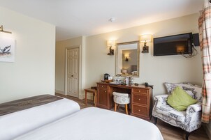 Quarto de hotel com duas camas, uma escrivaninha de madeira, uma cadeira, uma televisão e um espelho.
