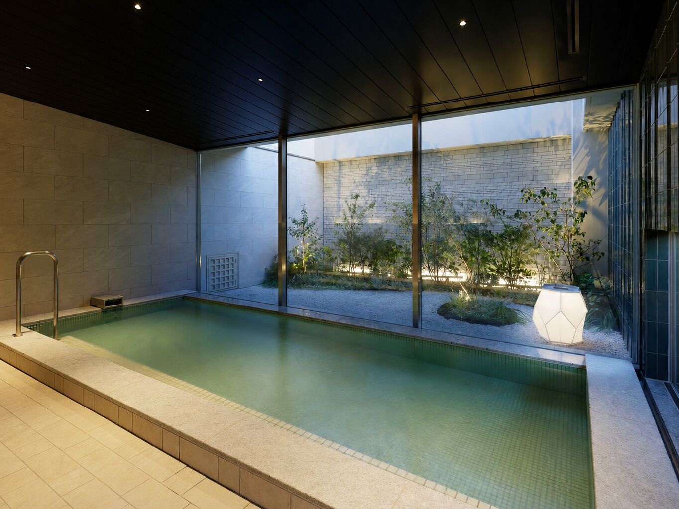 Uma piscina interior moderna com vista clara para a arquitetura circundante e uma pequena área ajardinada.